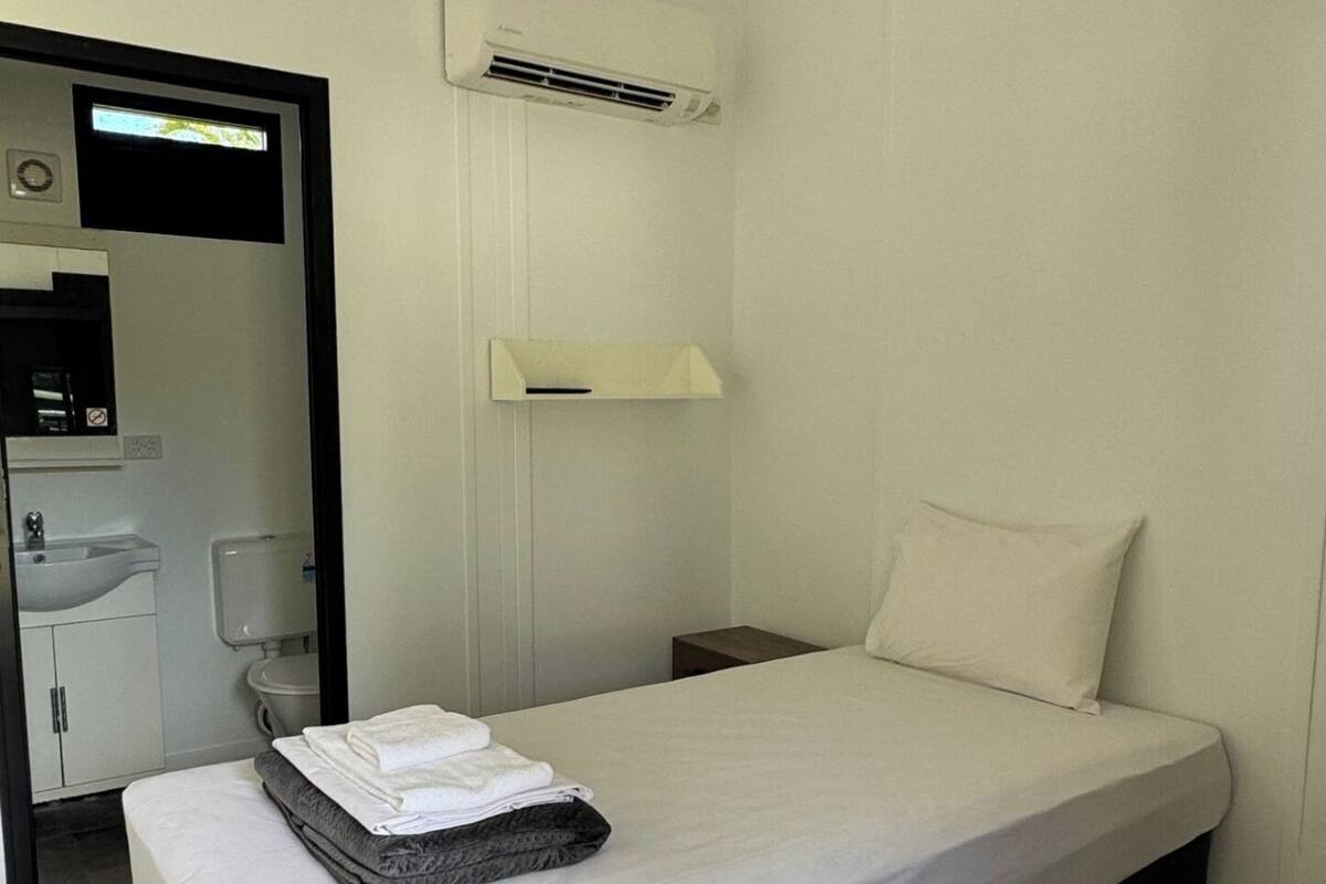 Quarto de hotel com cama, mesa de cabeceira, espelho, pia e ar condicionado.