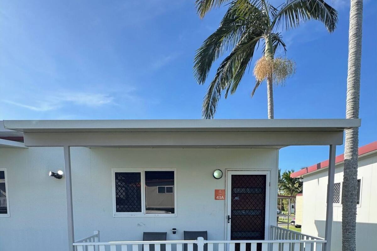 Um pequeno edifício térreo com fachada branca e varanda com guarda-corpo branco.