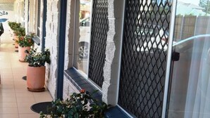 Uma galeria coberta com plantas em vasos, paredes de pedra e janelas com grades de metal.