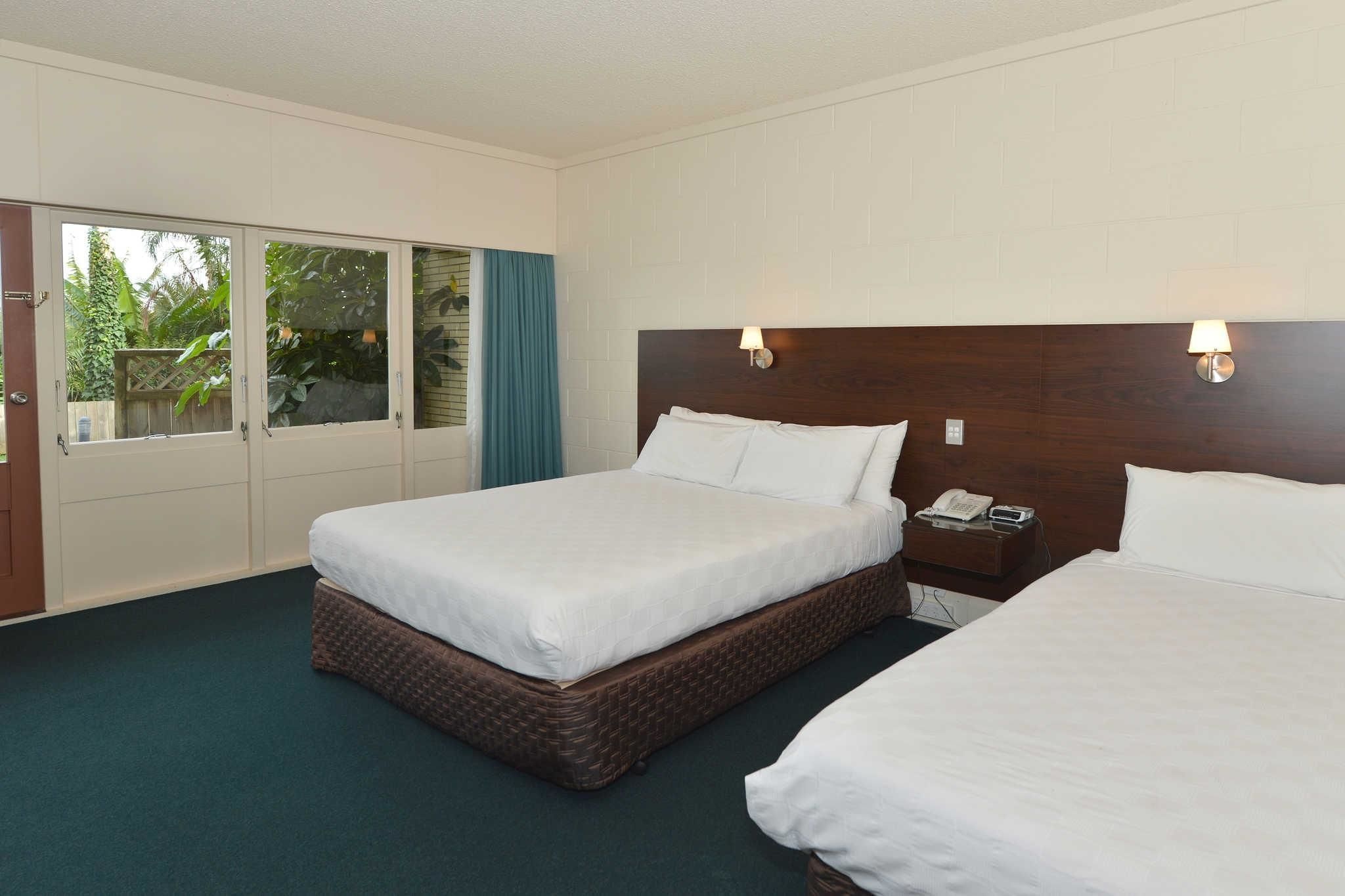 Quarto de hotel com duas camas, cabeceira de madeira, telefone e porta de vidro deslizante que dá para uma varanda.
