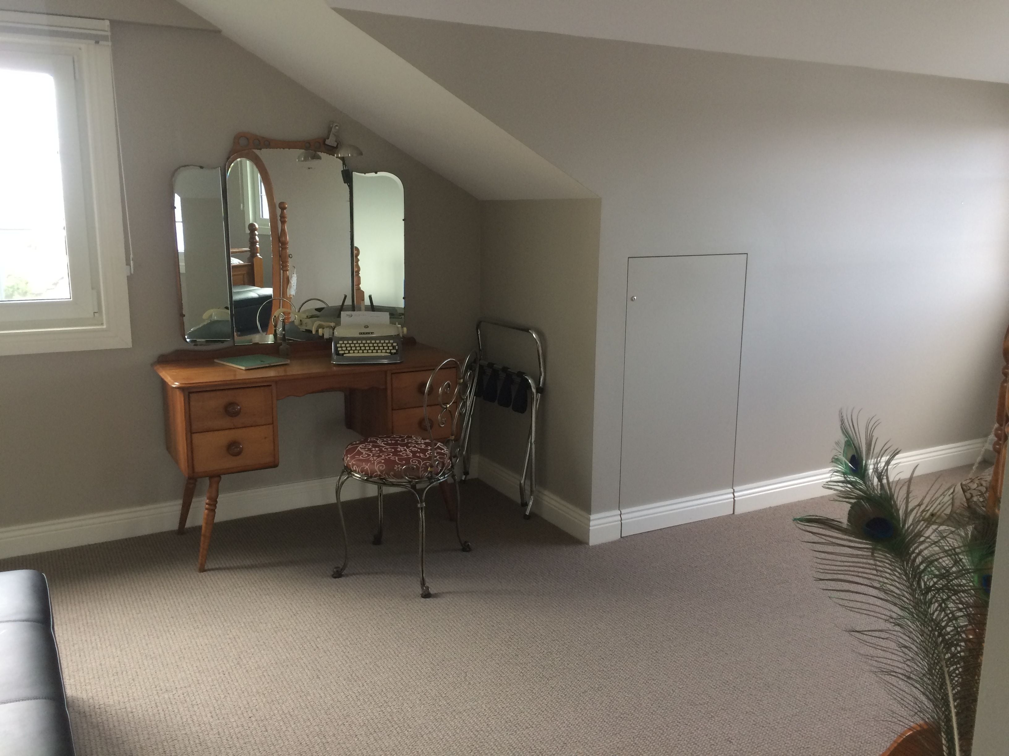 Quarto com escrivaninha de madeira, cadeira, espelho, guarda-roupa e decoração com pena de pavão.