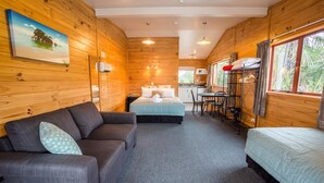Quarto aconchegante em estilo cabana, com cama, sofá, escrivaninha e janela com vista para o verde.