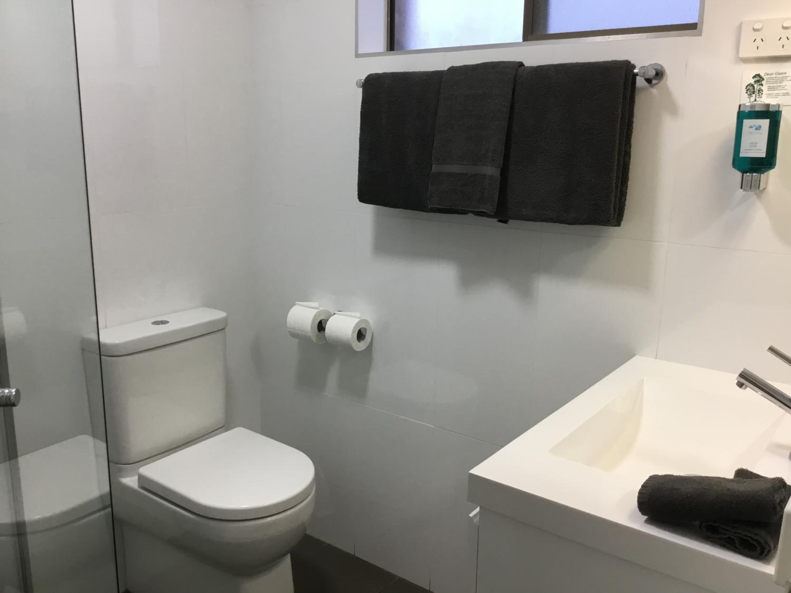 Casa de banho com sanita, lavatório e um porta-toalhas com duas toalhas.