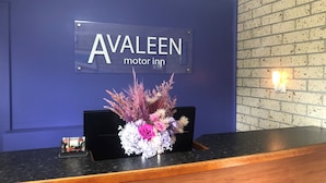 Uma receção com uma placa a indicar "AVALEEN motor inn" e um arranjo floral no balcão.