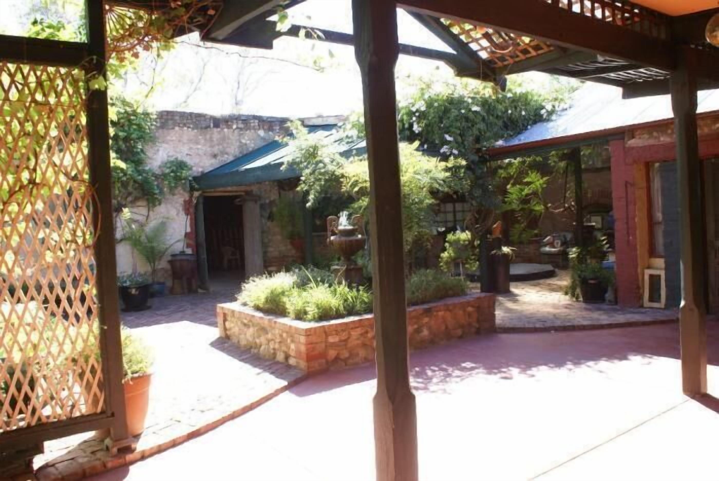 Uma área de pátio externa com vasos de pedra, uma pérgola e vista para um edifício com telhado azul.