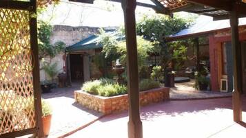 Uma área de pátio externa com vasos de pedra, uma pérgola e vista para um edifício com telhado azul.