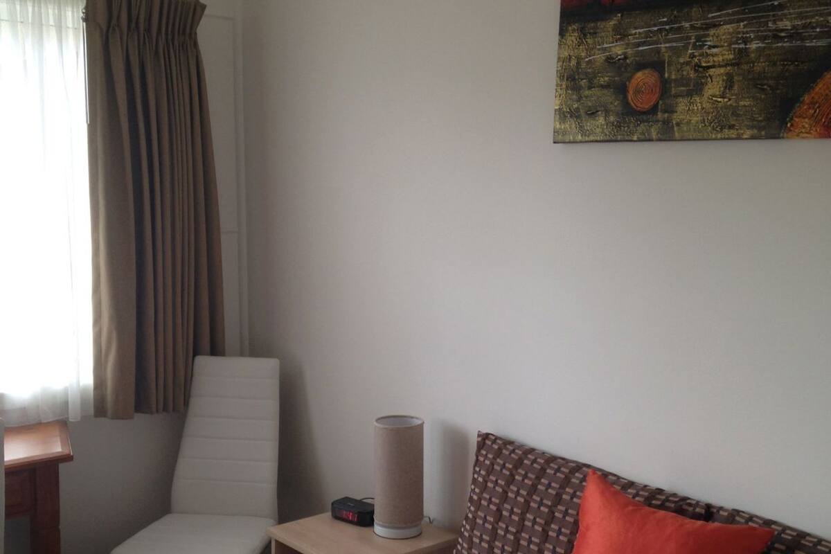 Quarto de hotel com cama, cadeira, mesa de cabeceira e uma obra de arte na parede.