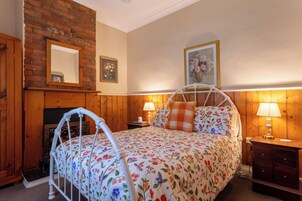 Quarto com estrutura de cama de madeira, roupa de cama floral, lareira e mesa de cabeceira com abajur.