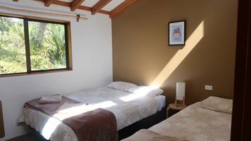 Quarto com duas camas de solteiro, janela com vista para área verde, quadro na parede e mesa de cabeceira com abajur.