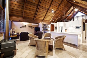 Uma sala de estar ampla com teto alto, lareira, móveis de vime e cozinha moderna.