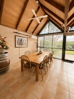 Uma sala de jantar com mesa e cadeiras de madeira, um ventilador de teto e uma janela grande com persianas.