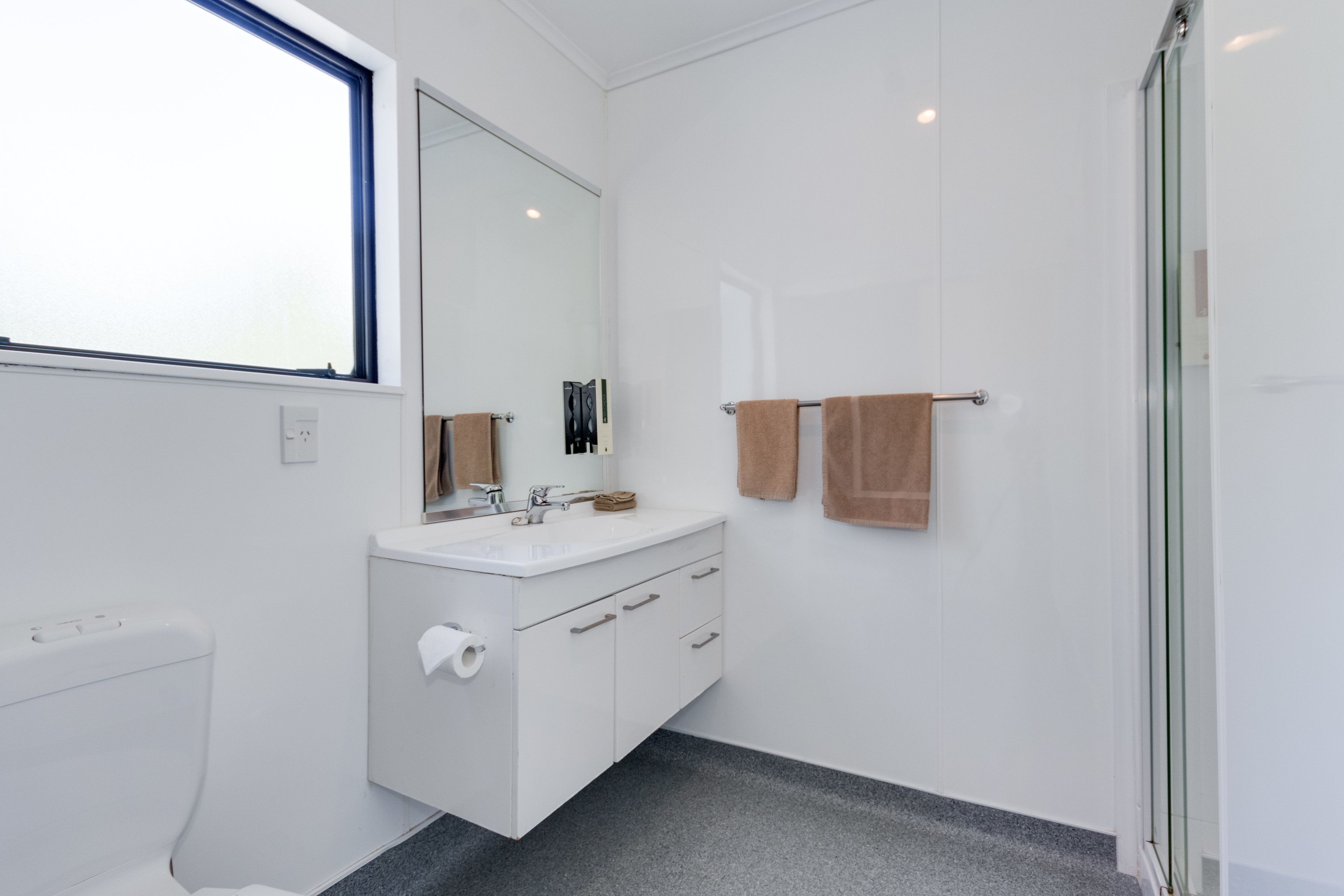 Casa de banho moderna com toucador branco, espelho grande e cabine de duche em vidro.