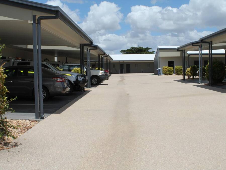 Uma área de estacionamento com vagas cobertas e um edifício ao fundo.