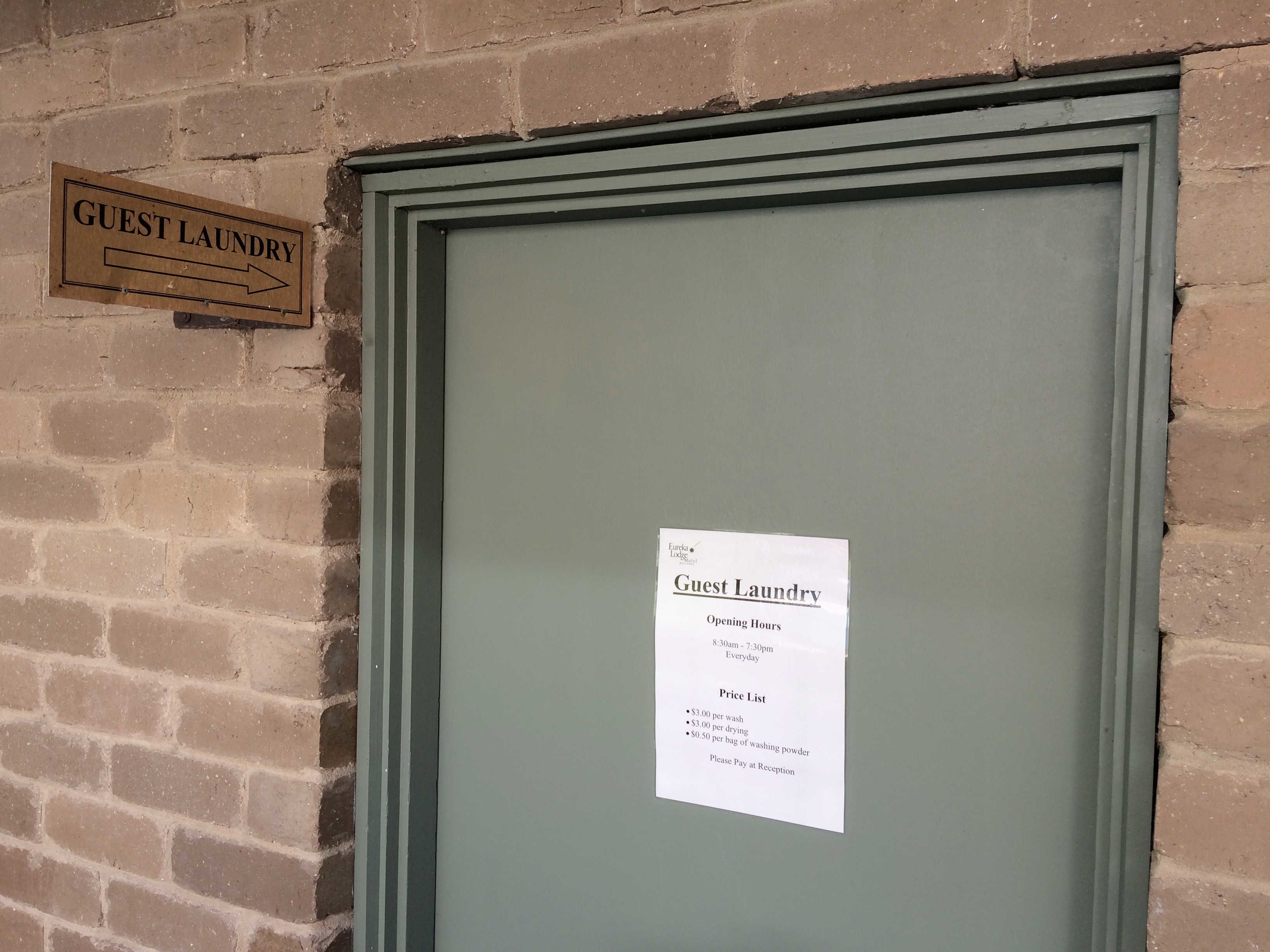 Sinal de lavanderia para hóspedes e porta com aviso indicando horário e preços do serviço de lavagem.