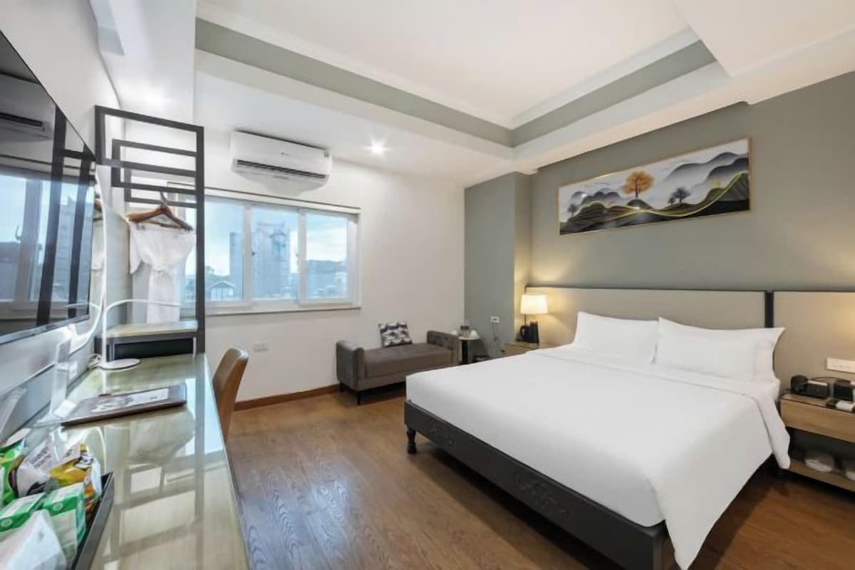 Quarto de hotel com uma cama grande, uma escrivaninha com espelho, um sofá e um quadro na parede.