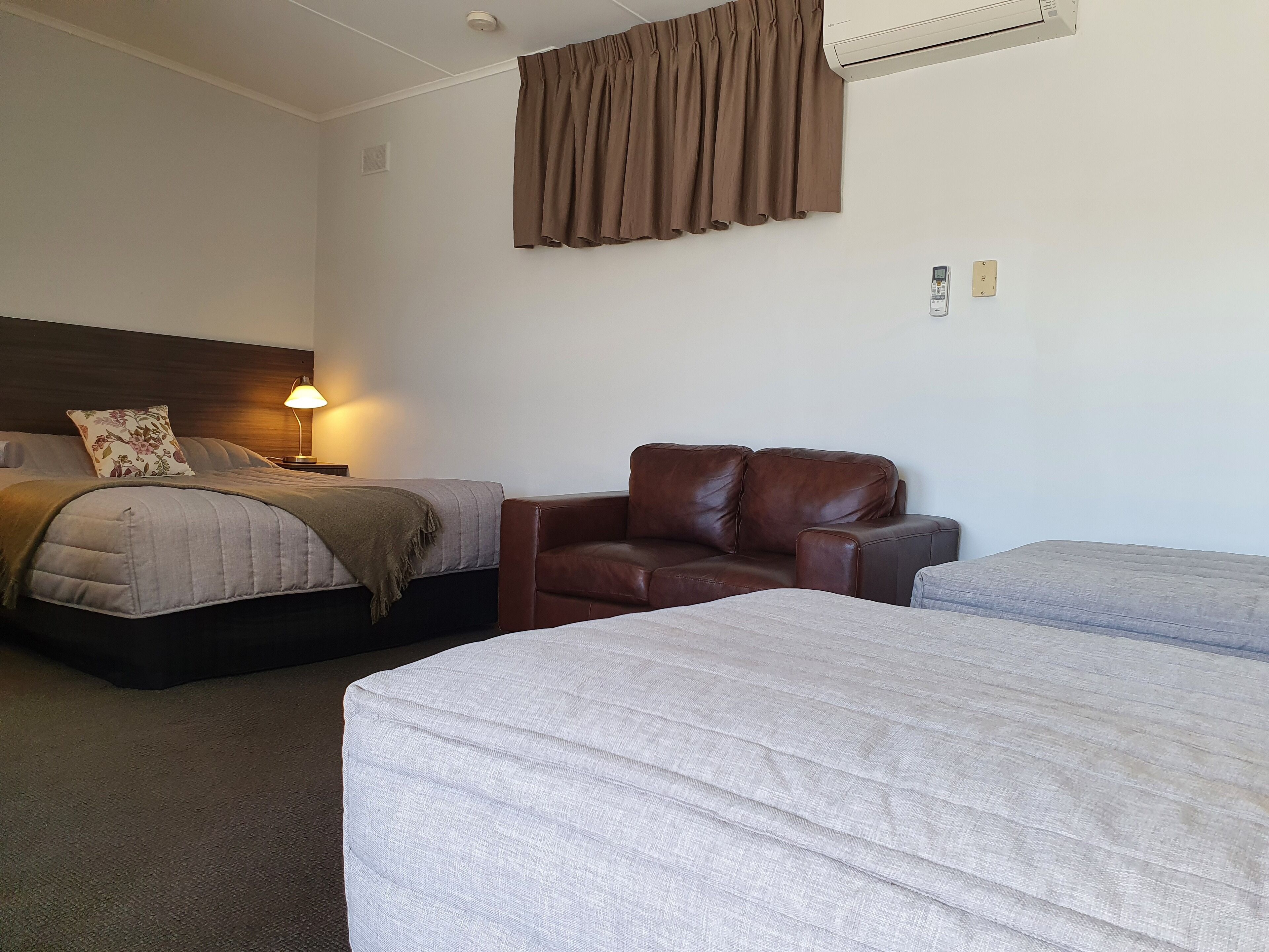 Quarto de hotel com cama, sofá, mesa de cabeceira com abajur e ar condicionado.