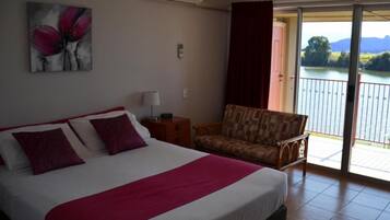 Quarto de hotel com uma cama grande, uma cadeira, um quadro e vista para um corpo de água.