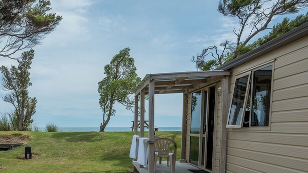 Uma casa térrea com varanda coberta, vista para o mar e um gramado.