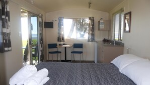 Quarto com cama, duas cadeiras, uma mesinha, pia e janela com cortinas.