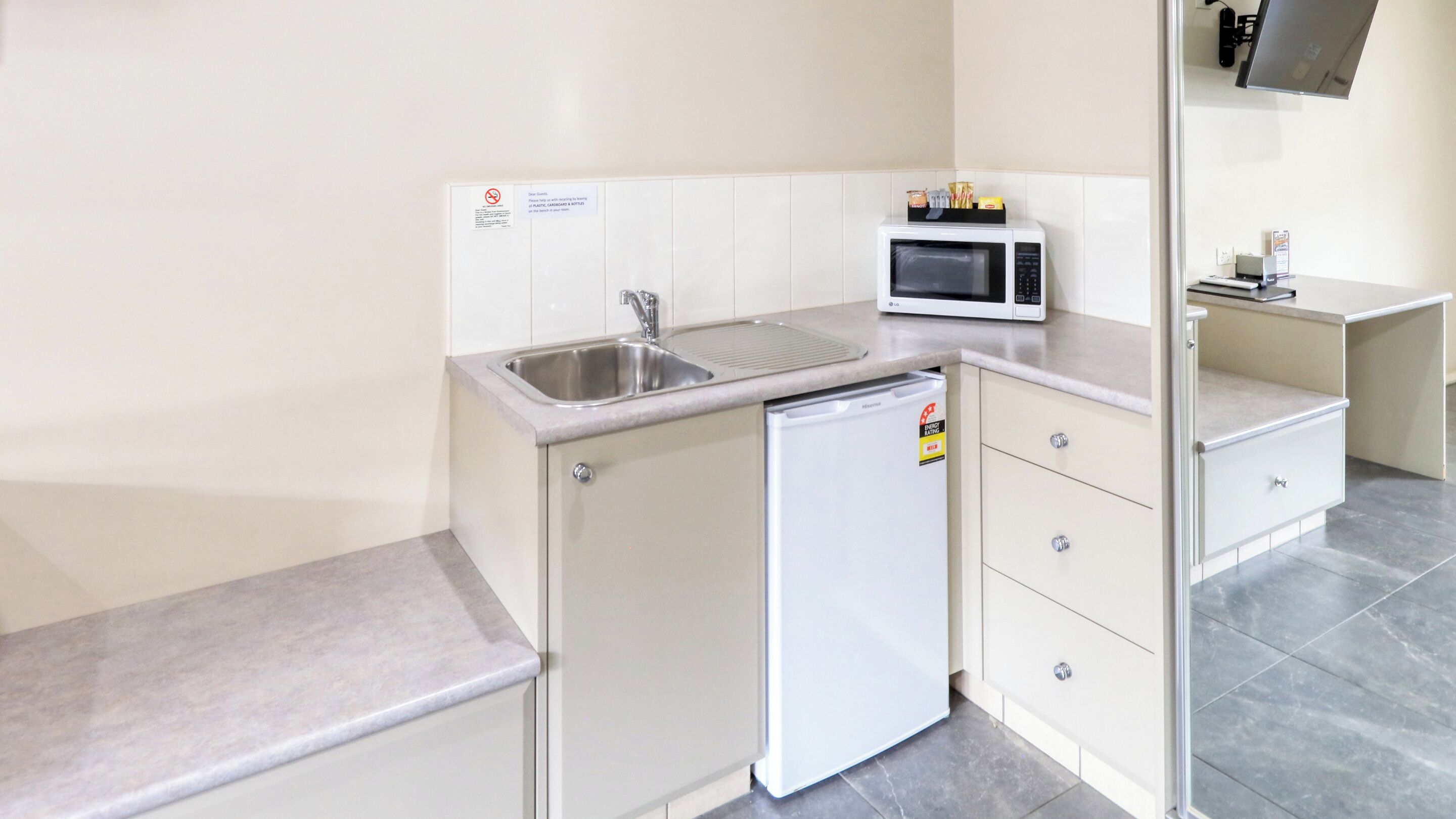Uma cozinha compacta equipada com pia de aço inoxidável, micro-ondas e pequeno frigorífico.