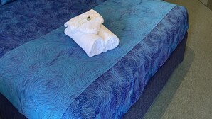 Quarto de hotel com uma cama grande, uma mesa de cabeceira com abajur, uma cadeira e uma pequena mesa.