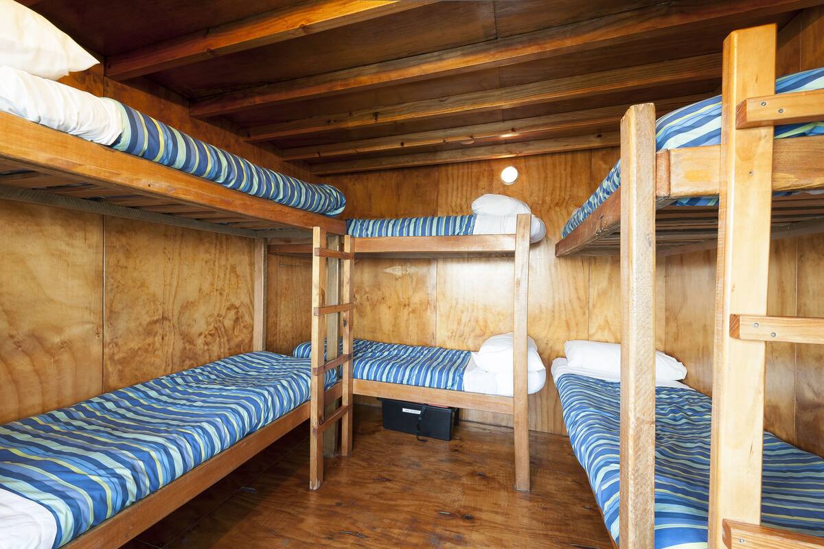 Quarto com beliches de madeira, paredes e pisos, com três beliches e roupa de cama listrada.