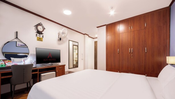 Quarto de hotel com cama grande, guarda-roupa de madeira, secretária com computador e televisão.
