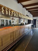 Uma longa área de bar com balcão de madeira, luzes pendentes e piso ladrilhado.