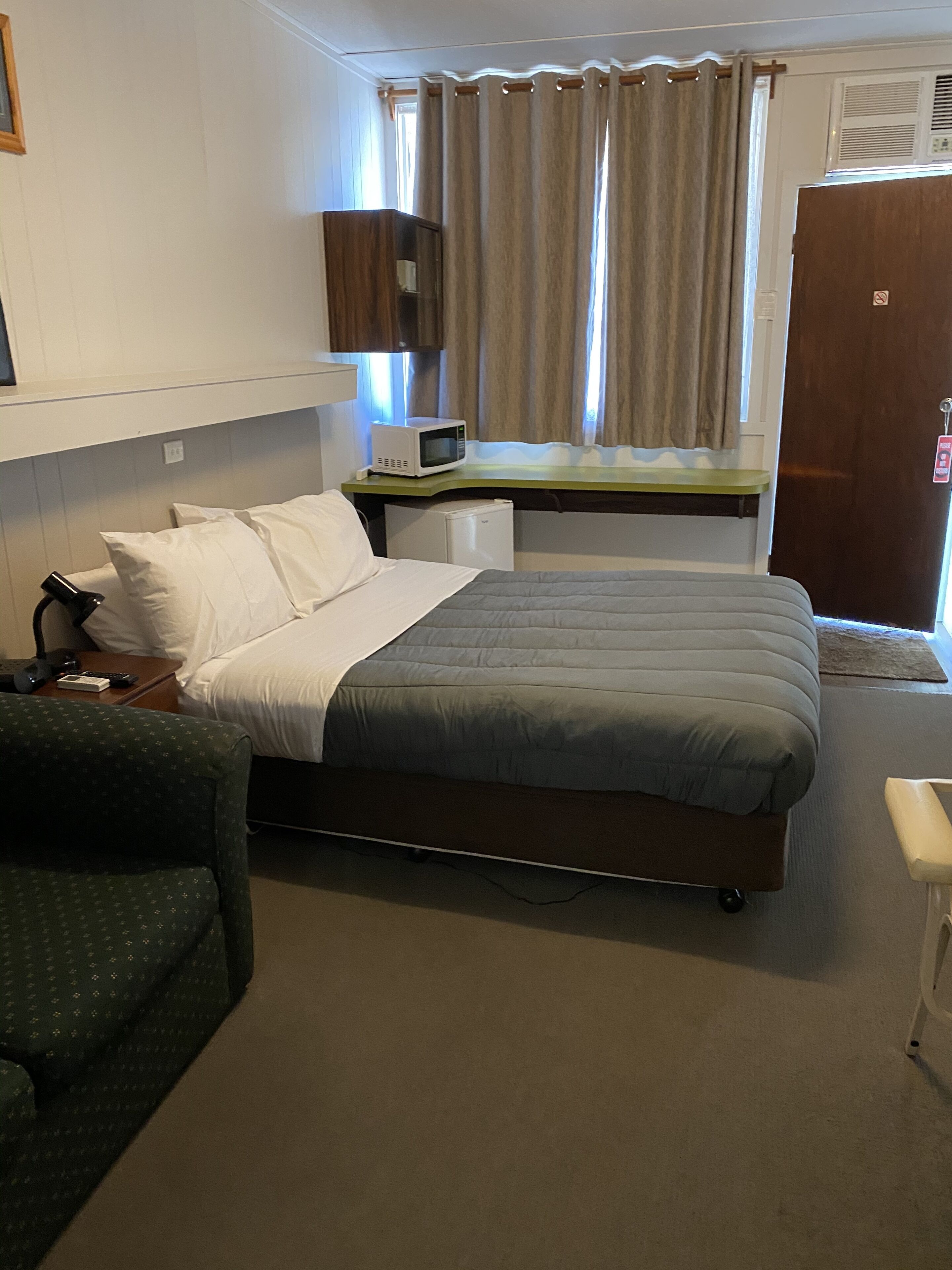 Quarto de hotel com cama, escrivaninha com micro-ondas, mini-frigorífico, cadeira e guarda-roupa.