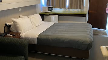 Quarto de hotel com cama, escrivaninha com micro-ondas, mini-frigorífico, cadeira e guarda-roupa.