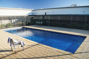 Piscina retangular com deck revestido e cerca de metal.