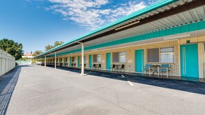 Um motel com área de estacionamento coberta e quartos individuais com portas numeradas.
