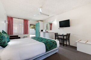 Quarto de hotel com cama, escrivaninha, cadeira, televisão e ventilador de teto.