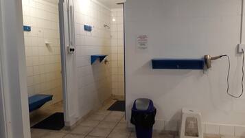 Um banheiro público com paredes de azulejos brancos, bancos azuis, uma lixeira e um pequeno banquinho.