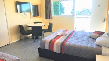 Quarto de hotel com cama, escrivaninha, cadeira, televisão e janela com cortinas.