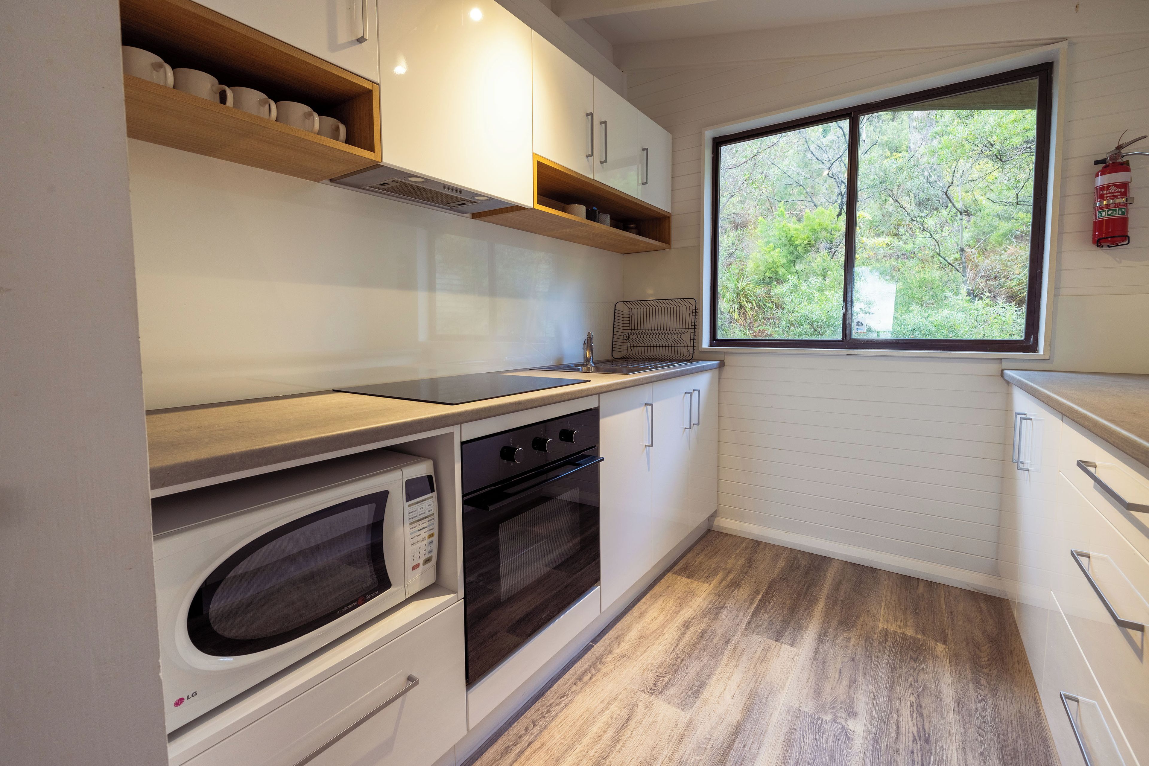 Cozinha moderna com armários brancos, forno embutido e janela com vista para o verde.