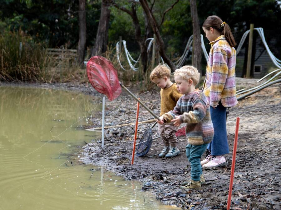 Três pessoas pescando em um corpo d'água lamacento com uma rede vermelha.