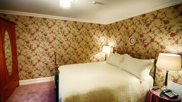 Uma cama bem arrumada com um edredom branco e almofadas, uma mesa de cabeceira com abajur e um guarda-roupa de madeira.