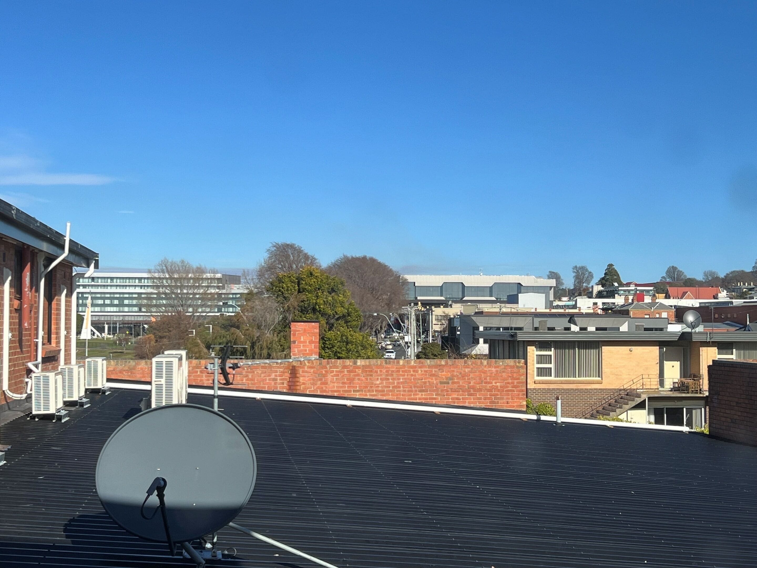 Terraço com antena parabólica, parede de tijolos e edifícios ao fundo.