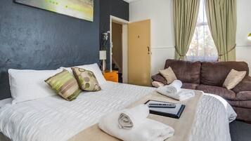 Quarto de hotel com cama, sofá marrom e janela com cortinas.