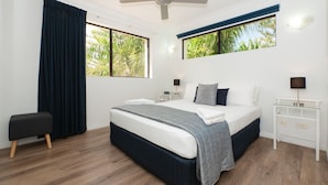 Quarto moderno com cama grande, mesas de cabeceira, escrivaninha e janela com vista para o verde.