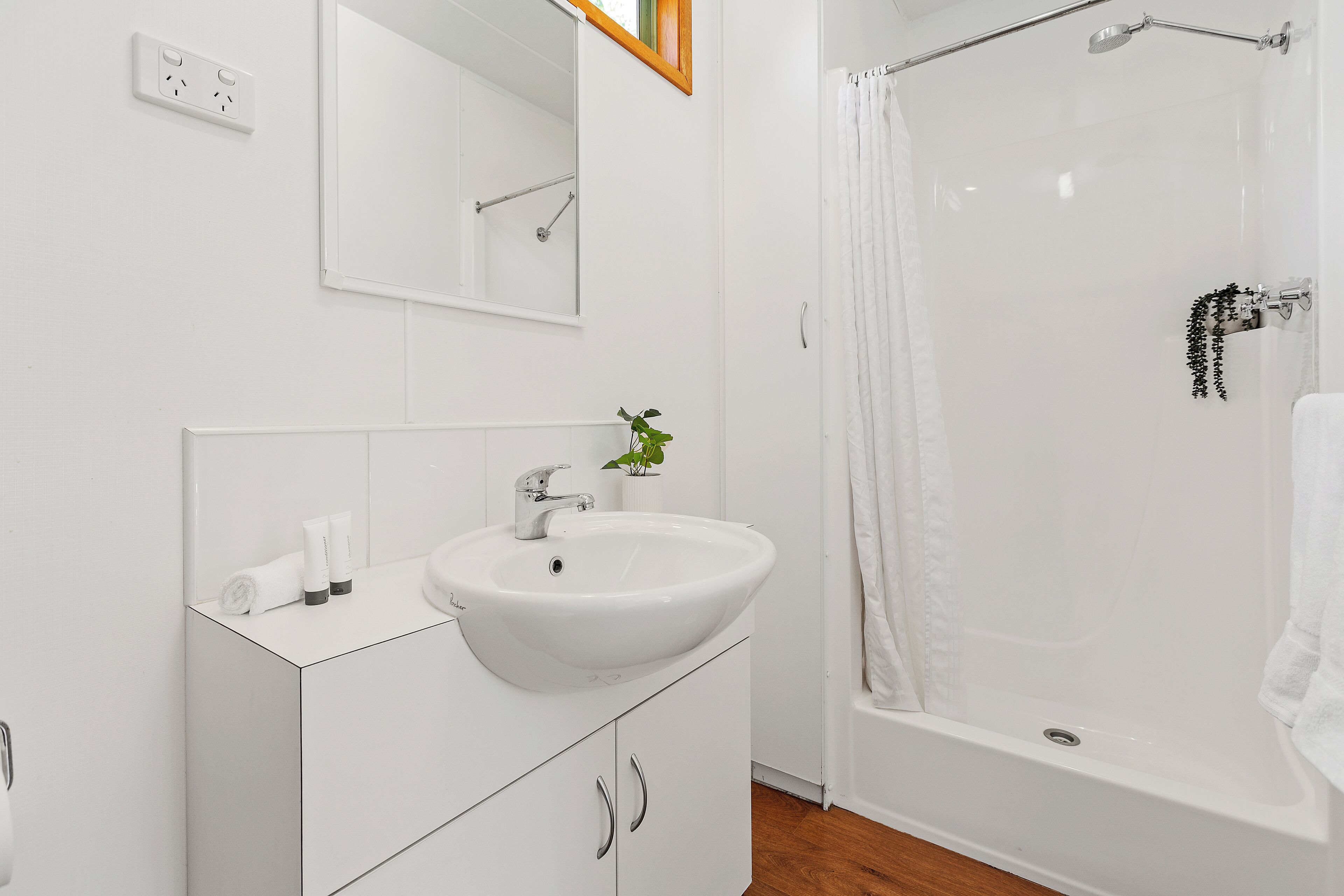 Casa de banho moderna com lavatório branco, espelho e chuveiro.