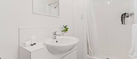 Casa de banho moderna com lavatório branco, espelho e chuveiro.