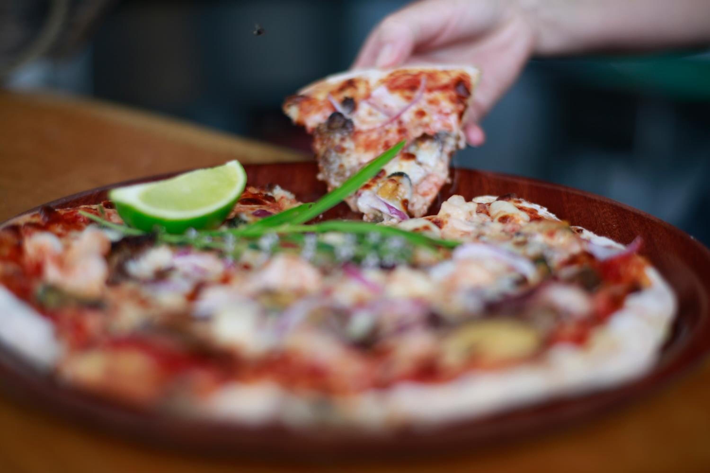 Pizza com cobertura e uma fatia de limão sobre uma mesa de madeira.