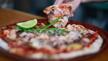 Pizza com cobertura e uma fatia de limão sobre uma mesa de madeira.