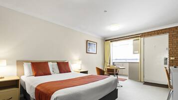 Quarto de hotel com cama, mesas de cabeceira, escrivaninha, cadeira, mesinha e um frigorífico.