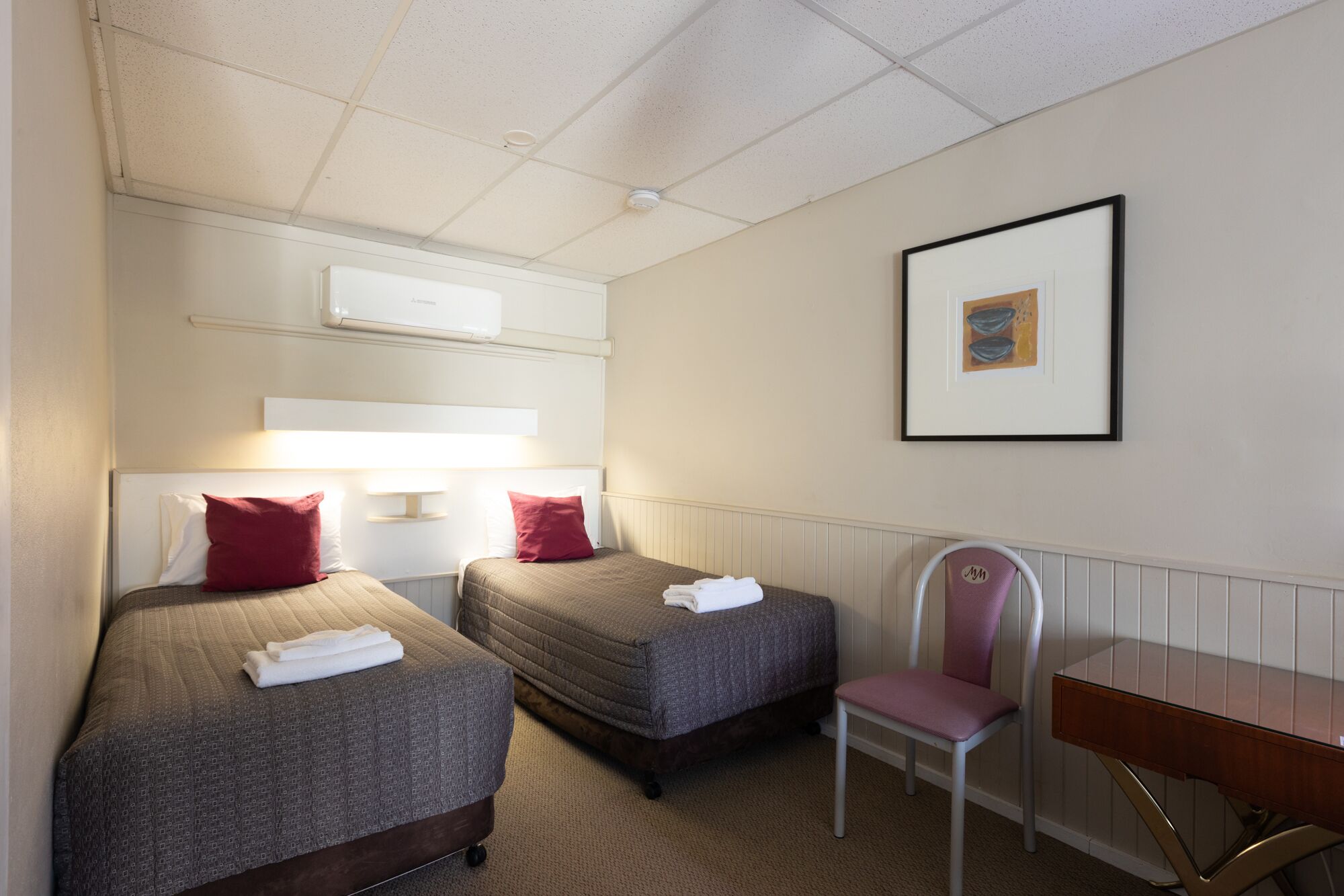 Quarto de hotel com duas camas, uma escrivaninha e uma cadeira.