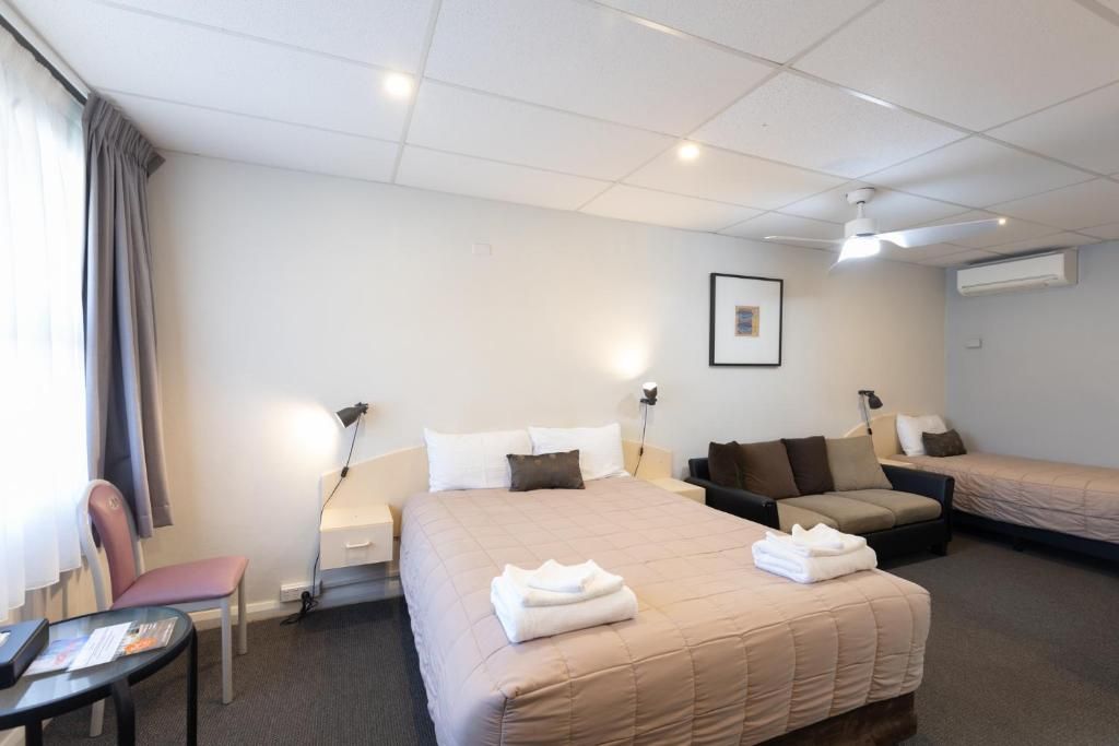 Quarto de hotel com uma cama grande, uma cama menor, uma escrivaninha, uma cadeira e uma mesinha de cabeceira.