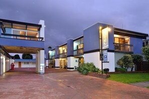 Um motel moderno com estrutura em dois andares, área de estacionamento coberta e placa indicando disponibilidade para estadias curtas.