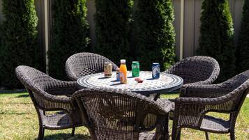 Mesa redonda para exterior com cadeiras de vime, um refrigerador de bebidas e uma lata de refrigerante.